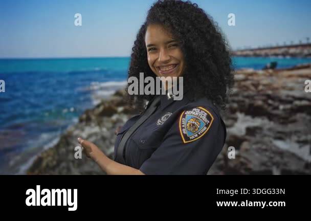 Smiling young police officer with curly hair extends hands backwards ...