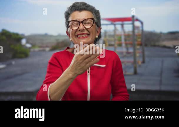 Senior woman laughing on an urban street with playful gestures, wearing ...