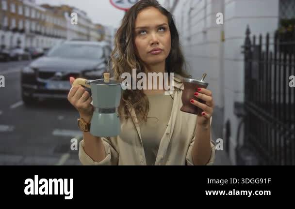 Woman holding a coffee maker and cup outdoors on a city street displays ...