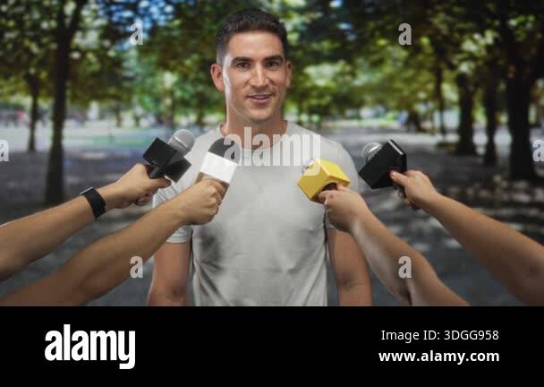 Man wearing white t shirt with microphones held by multiple hands on a ...