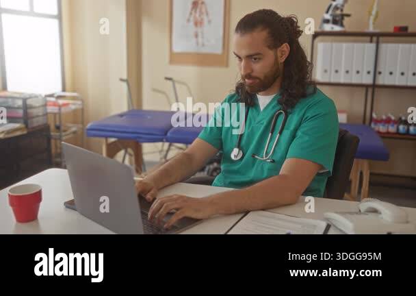 Young man doctor in green scrubs with stethoscope typing on laptop at ...