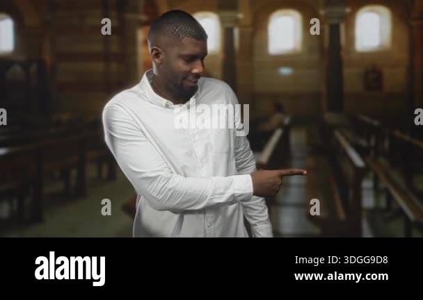 Young man points finger to right in a church aisle beside wooden pews ...