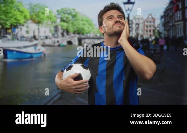 Young hispanic man holding a soccer ball and touching his cheek with ...