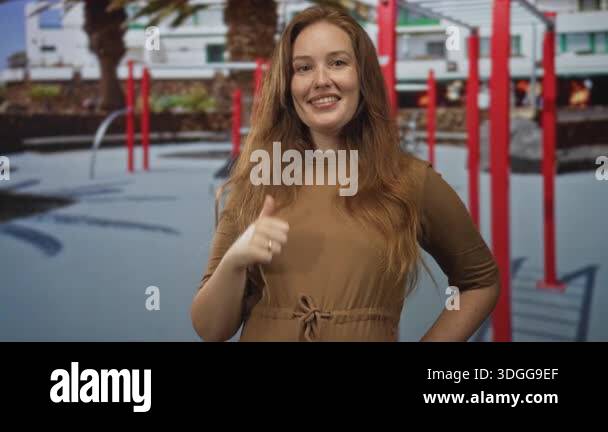 Woman leans on red gym bars and gives thumbs up while looking off ...