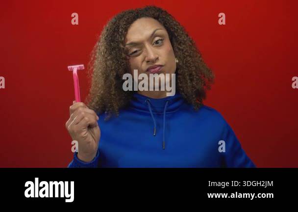 Woman holding pink razor close to face with hand on cheek in red studio ...