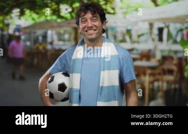 Hispanic man celebrating outdoors on a street, holding a soccer ball ...