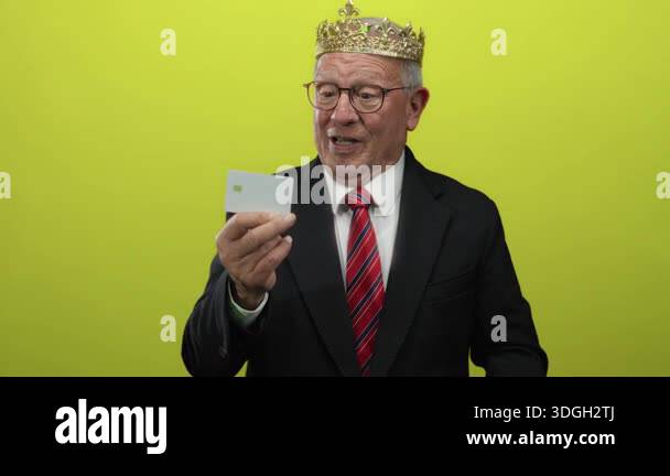 Senior man wearing a crown holds a blank credit card and gestures ...