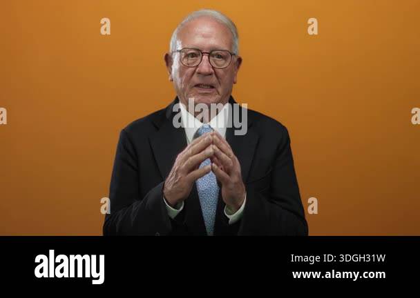 Senior man in a suit isolated against an orange background, displaying ...