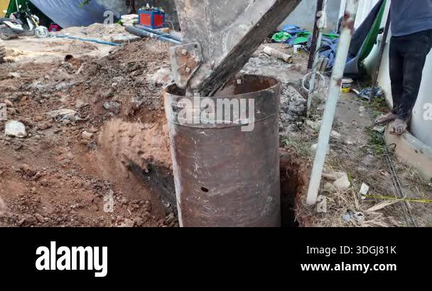 close up of an excavator bucket guiding a large metal piling casing at ...