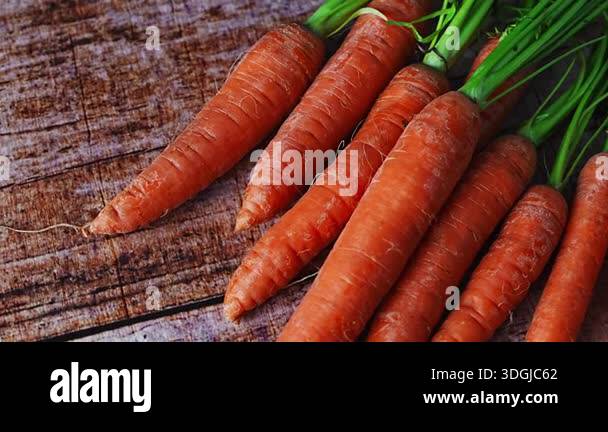 Bunch of fresh raw carrots with green tops lying on wooden wooden table ...