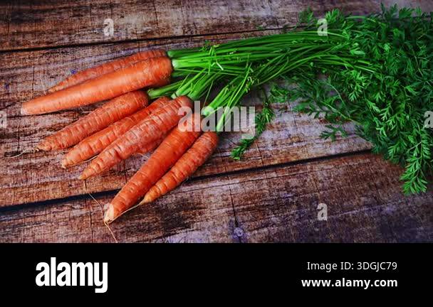 Bunch of fresh raw carrots with green tops lying on wooden wooden table ...