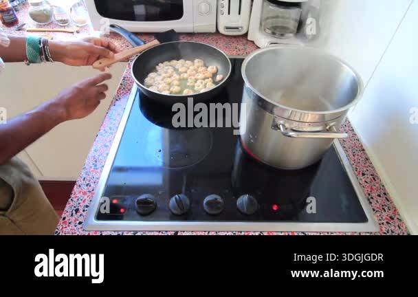 Closeup of person cooking pasta and frying shrimps on electric stove ...