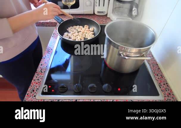Closeup of person cooking pasta and frying shrimps on electric stove ...