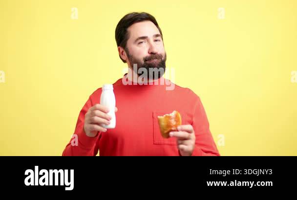 Happy bearded man eating delicious bun and drinking yogurt on a yellow ...