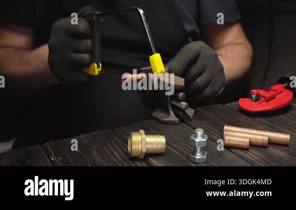 A person is using a saw to cut a copper pipe while it is held in a vise ...