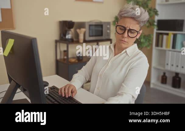 Woman seated at office desk touches forehead while looking at ...