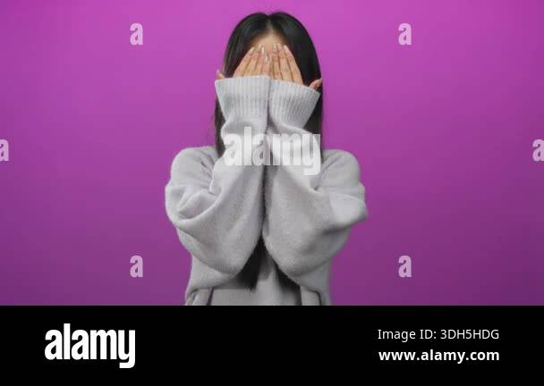 Young chinese woman playfully hiding face over isolated pink background ...