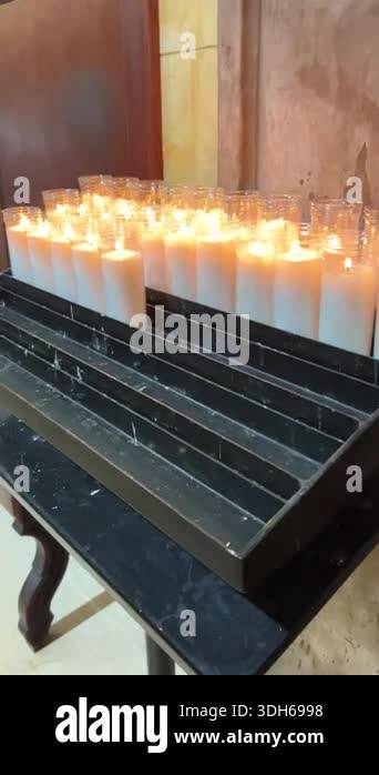Row of white devotional candles burning in glass holders inside a ...