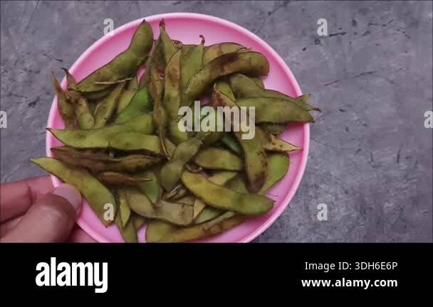Footage of a human hand holding green edamame beans on a pink plate. A ...