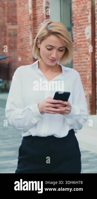 Beautiful woman standing near modern building typing text messages on ...