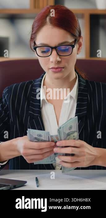 Woman in suit counting dollar bills and looking at camera while sitting ...