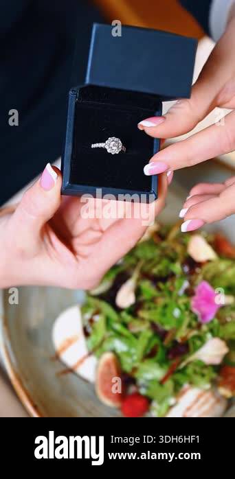 Person holding ring box while another hand holds ring near salad ...