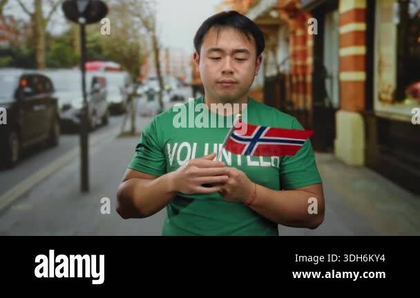 Young asian man holding a norwegian flag on a city street, playfully ...