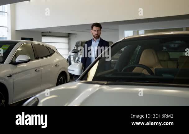 Rich Caucasian business man choosing modern electric car in dealership ...