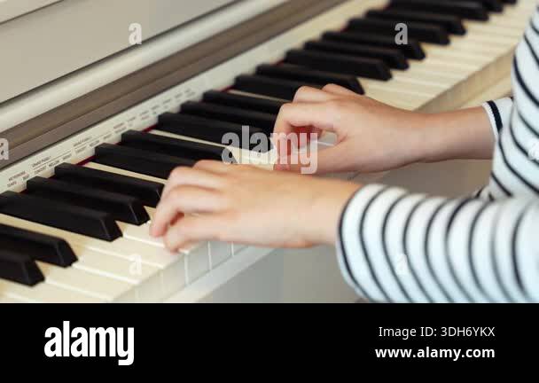 A person practices playing piano in a well-lit room. The hands move ...
