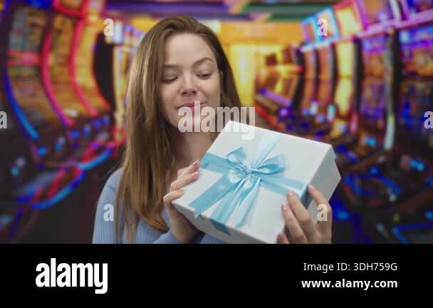 Woman holding light blue gift box with ribbon in casino next to slot ...