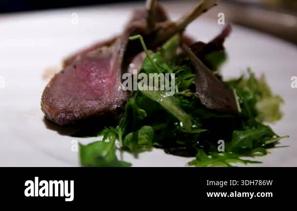 Pink sauce poured on rack of lamb in faience plate with salad and ...