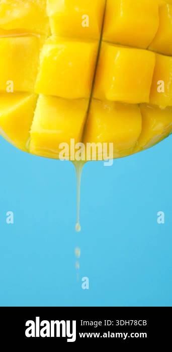 Mango juice slowly dripping from fresh fruit, blue background, vertical ...