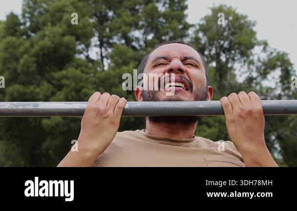 Man performing pull ups on outdoor exercise bars with visible effort ...