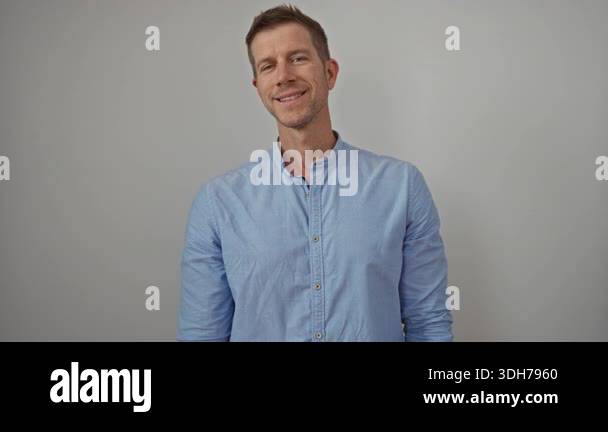 Young man smiling confidently in a blue shirt against a plain wall ...