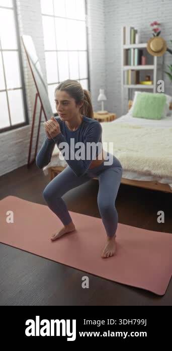 Woman exercising in bedroom performing squat on pink yoga mat wearing ...