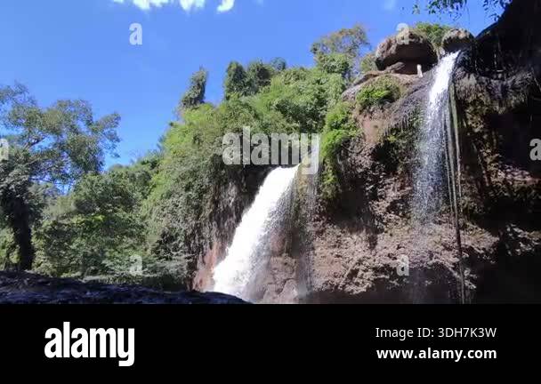 Stunning tropical waterfall cascading over a rocky cliff into a serene ...