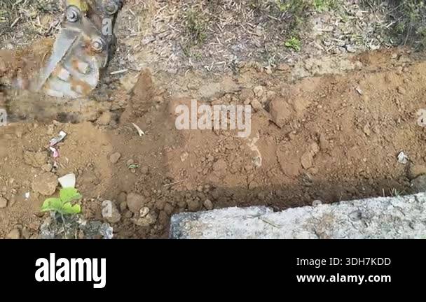An excavator uses its bucket to dig a narrow trench for laying pipes ...