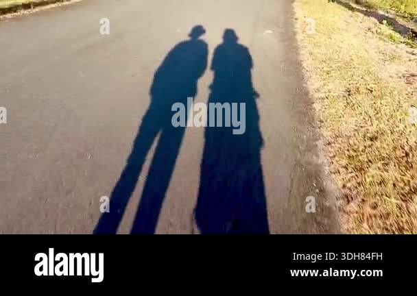 Shadows of two people walking together along a path as the sun nears ...