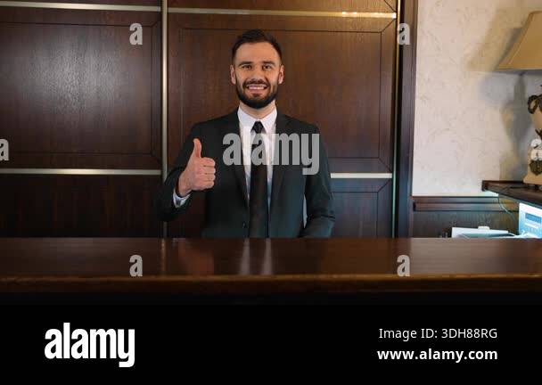 Positive young male hotel concierge with a beard, wearing a formal suit ...