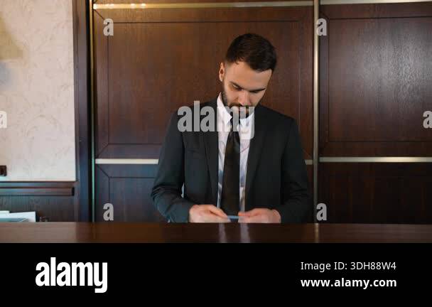 Friendly male receptionist in a suit working at the front desk. The ...