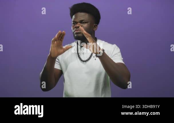 Man cupping hands to shout in studio purple wall wearing white tee and ...