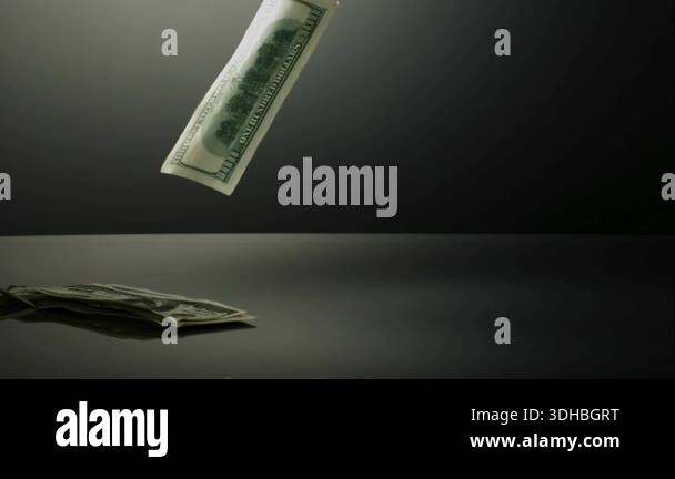 Single hundred dollar bill falling onto a dark reflective surface in ...
