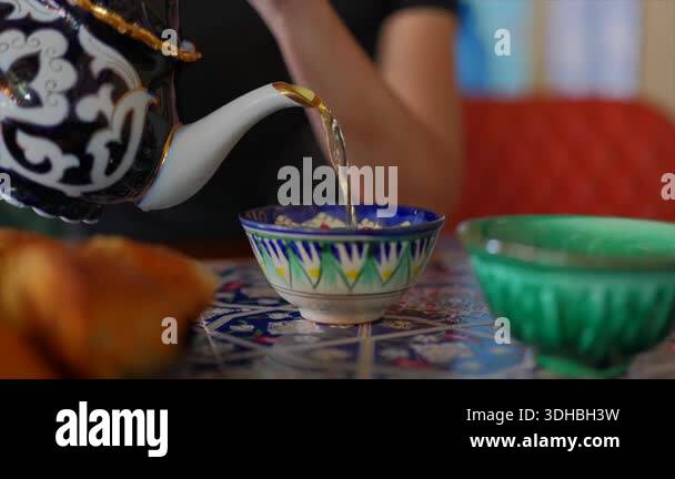 Green tea is poured from teapot into bowl in cozy Uzbek tea setting ...