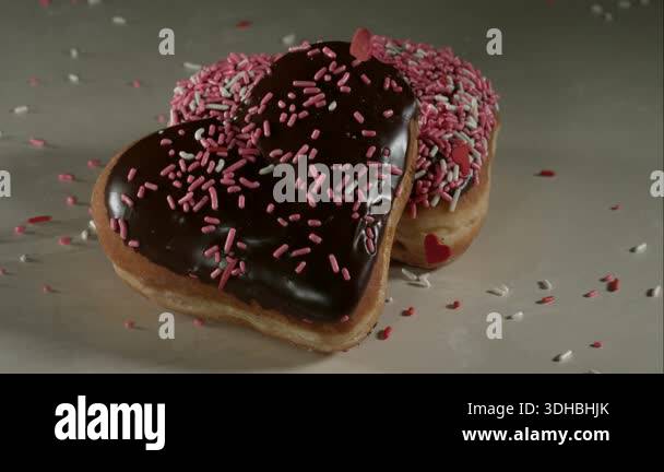 Two heart shaped donuts with chocolate and pink icing and sprinkles are ...
