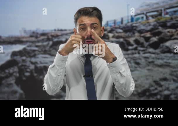 Man in white dress shirt and navy tie points finger at lip on rocky ...