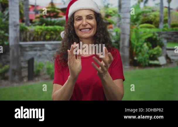 Woman clapping hands by green lawn in front of building wearing santa ...