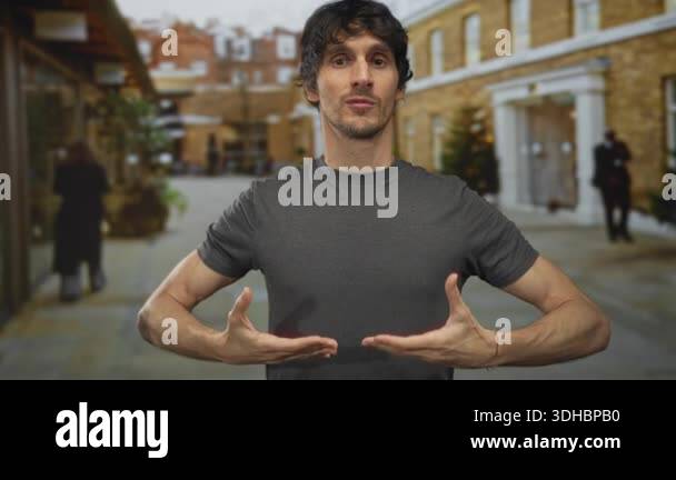 Young man in grey shirt leans forward and holds both hands at chest ...