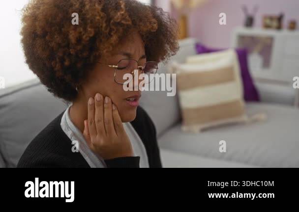 Woman with curly hair and glasses experiences tooth pain inside a cozy ...