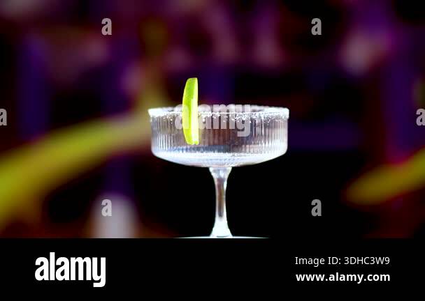 A vibrant pink margarita is poured into a glass with a lime slice, set ...