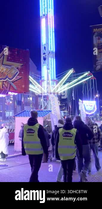 Tall illuminated swing ride spinning at a funfair with crowds of people ...